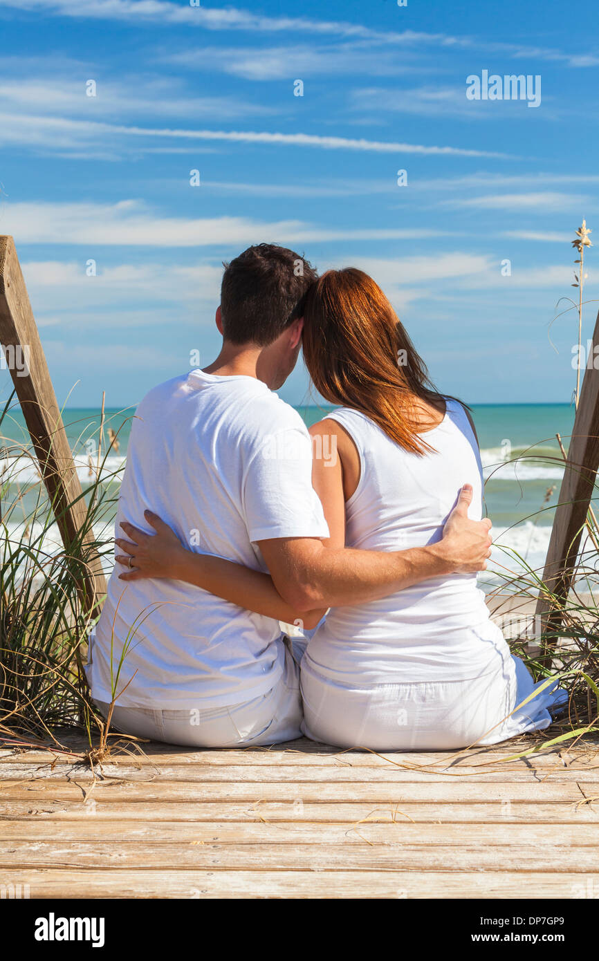 Rear view of romantic man & woman couple sitting on wooden steps ...