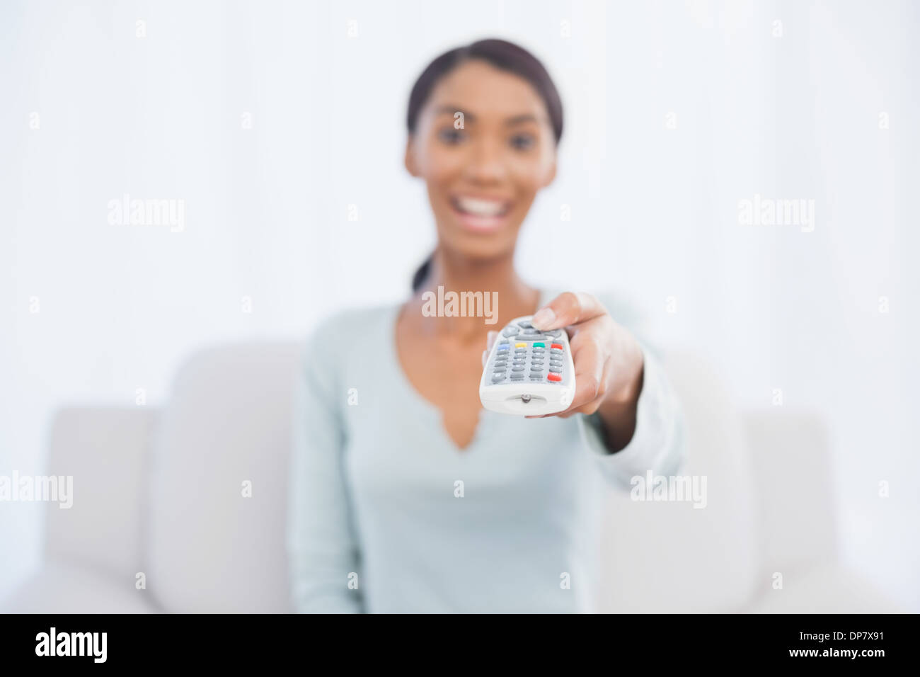 Cheerful pretty woman sitting on sofa changing tv channel Stock Photo ...