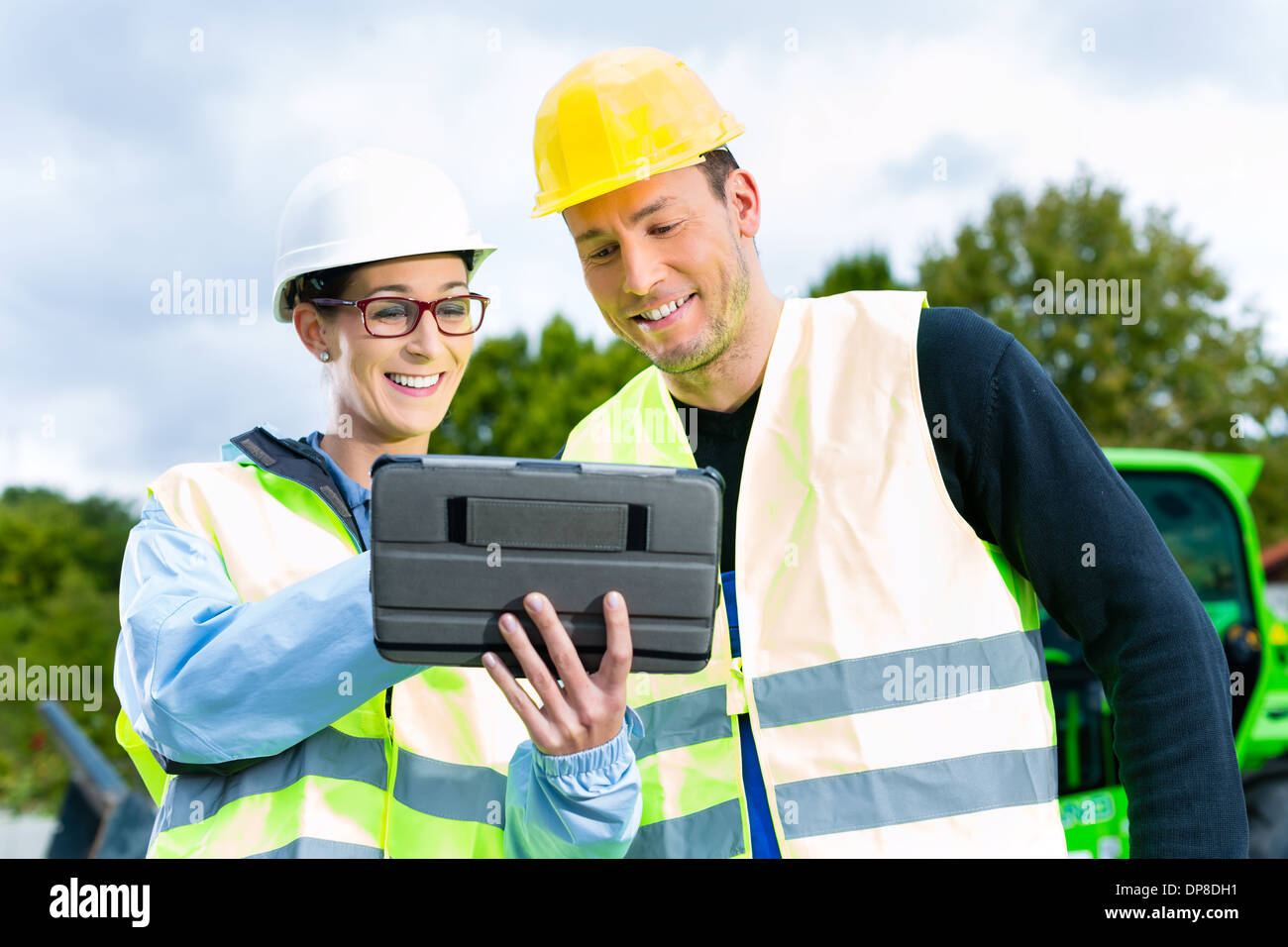 Construction worker and engineer on site discussing blueprints on pad ...