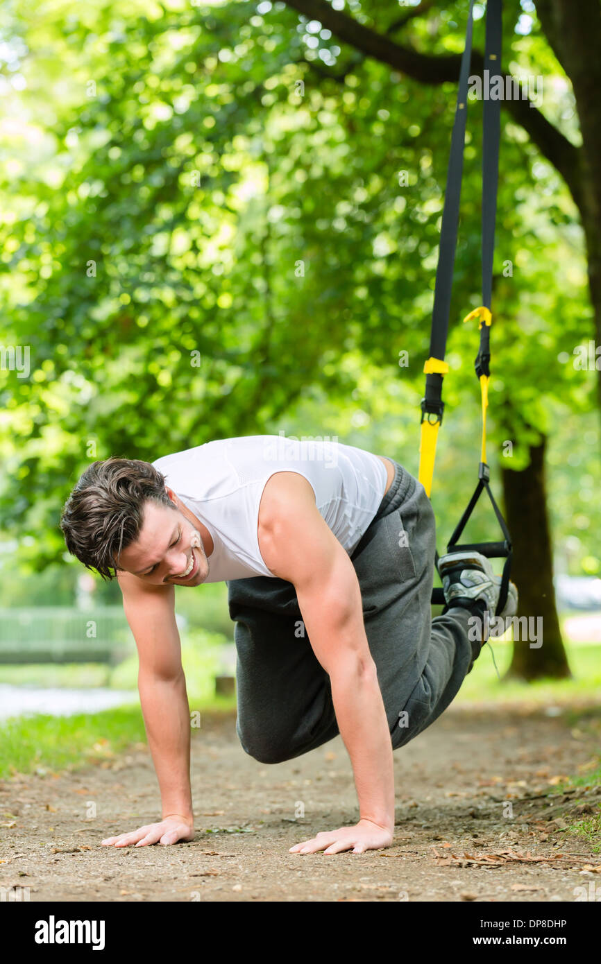 Young man exercising with suspension trainer sling in City Park under ...