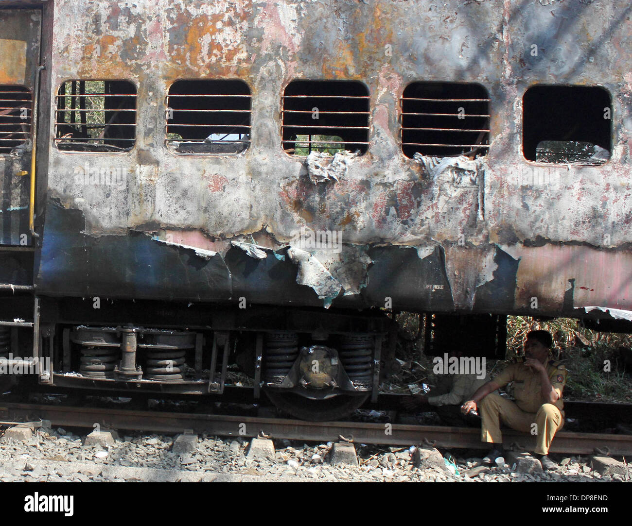Thane, India. 8th Jan, 2014. People sit under a burnt coach of Mumbai ...