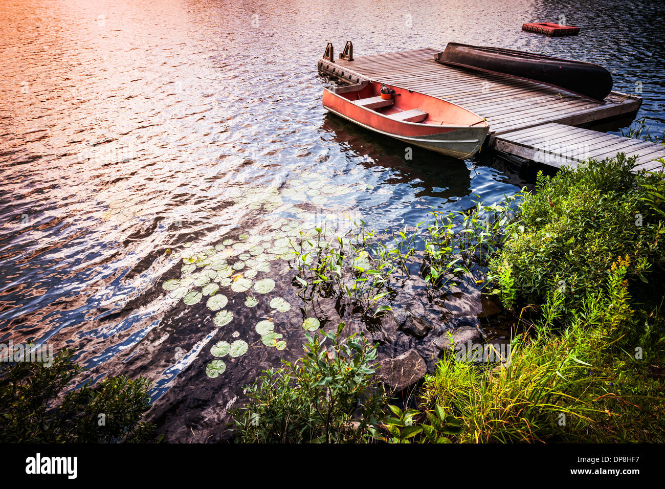 Sunset reflecting in lake water with rowboat tied to wooden dock at ...