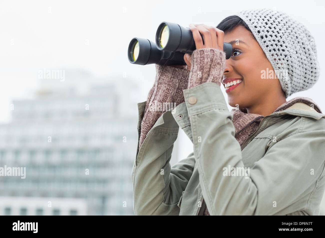 Pretty young model in winter clothes watching the city with binoculars ...