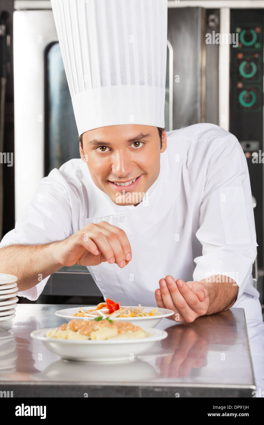 Happy chef sprinkling cheese on a pizza in a commercial kitchen Stock ...