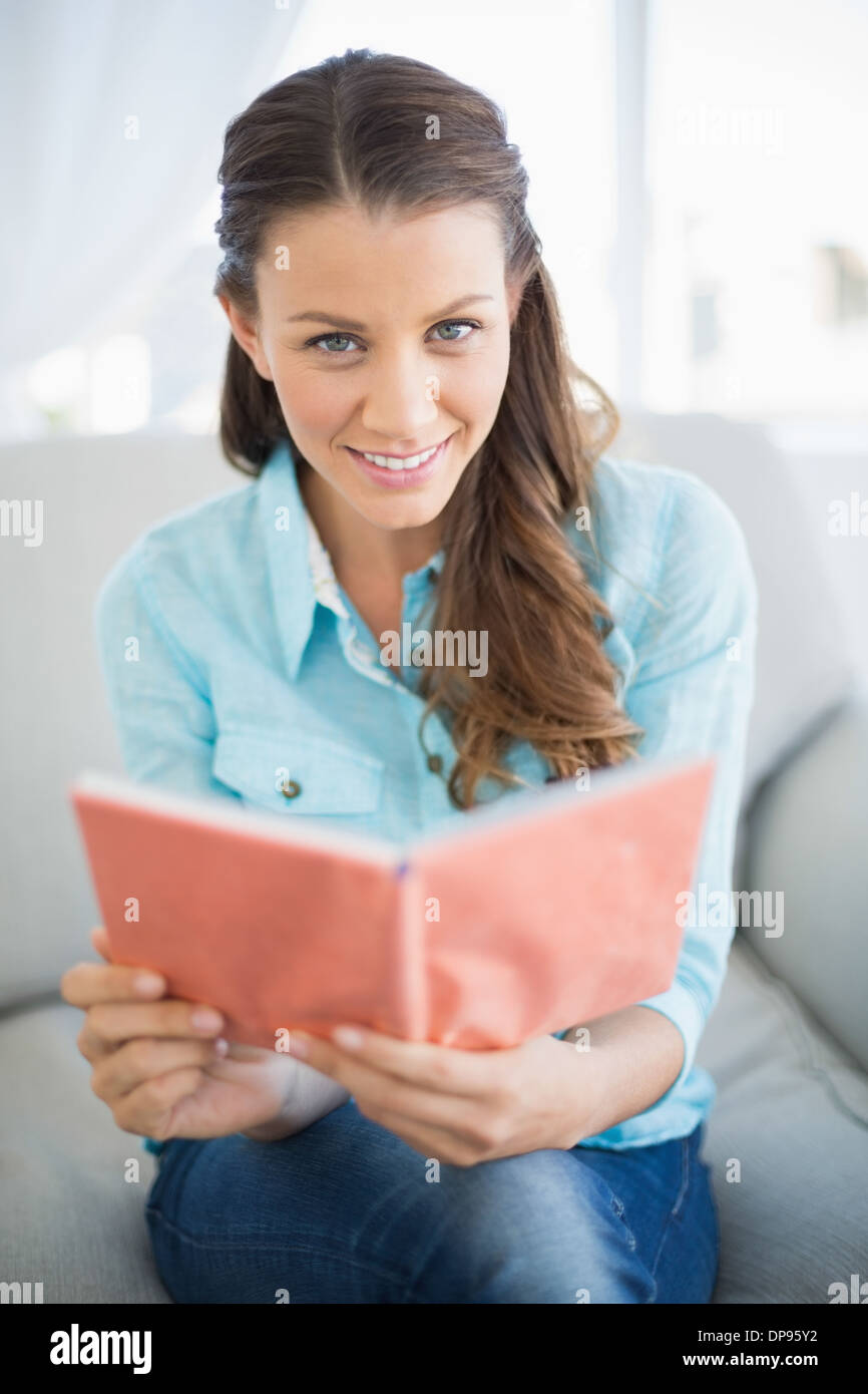 Smiling woman sitting on sofa reading book Stock Photo - Alamy