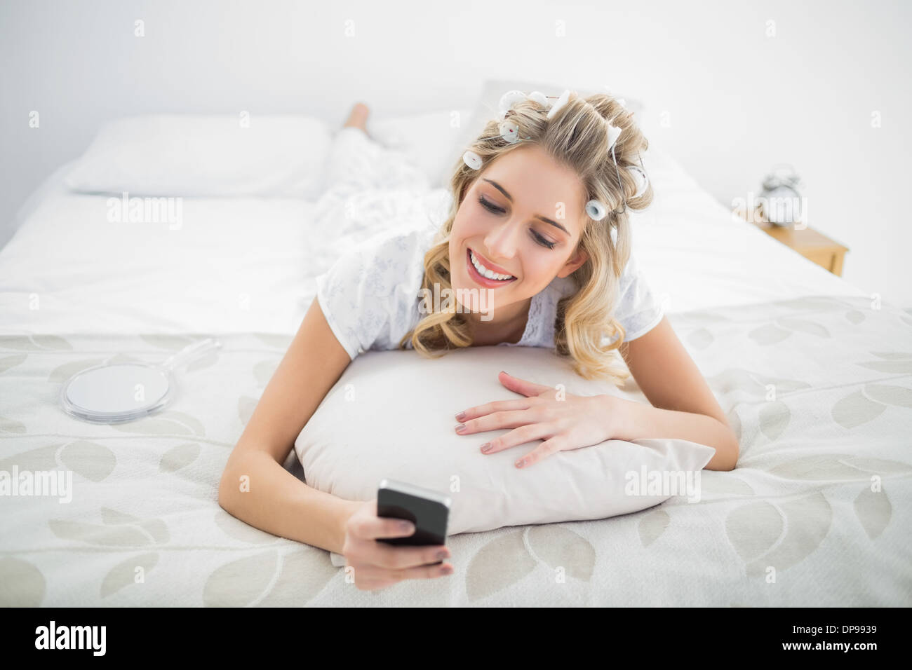 Peaceful blonde wearing hair curlers texting while lying on bed Stock ...
