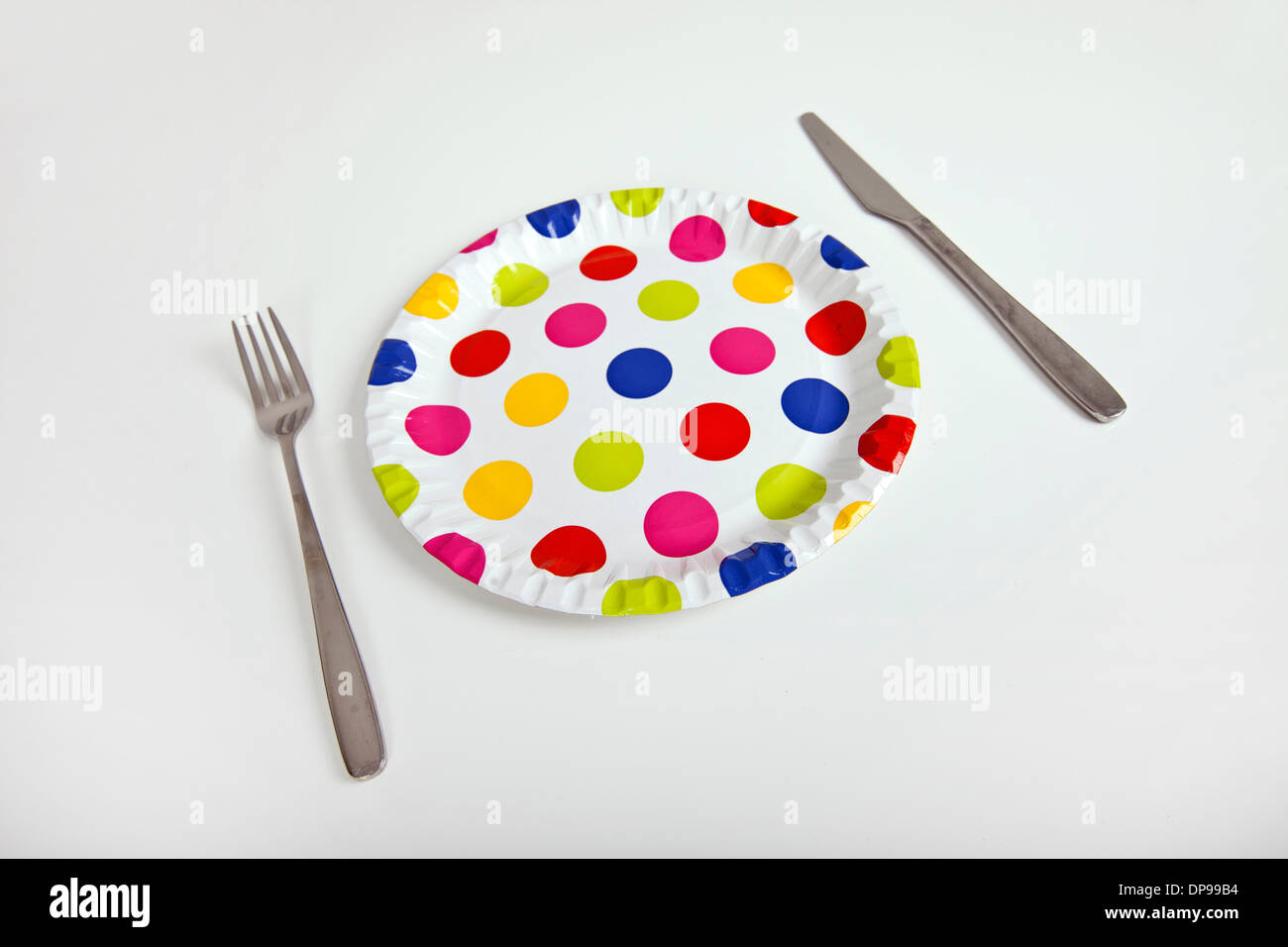 Multicolored plate with polka dots and cutlery over white background ...