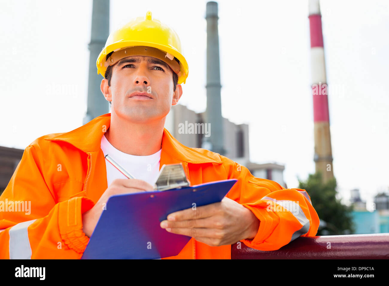 Male construction worker writing on clipboard at industry Stock Photo ...