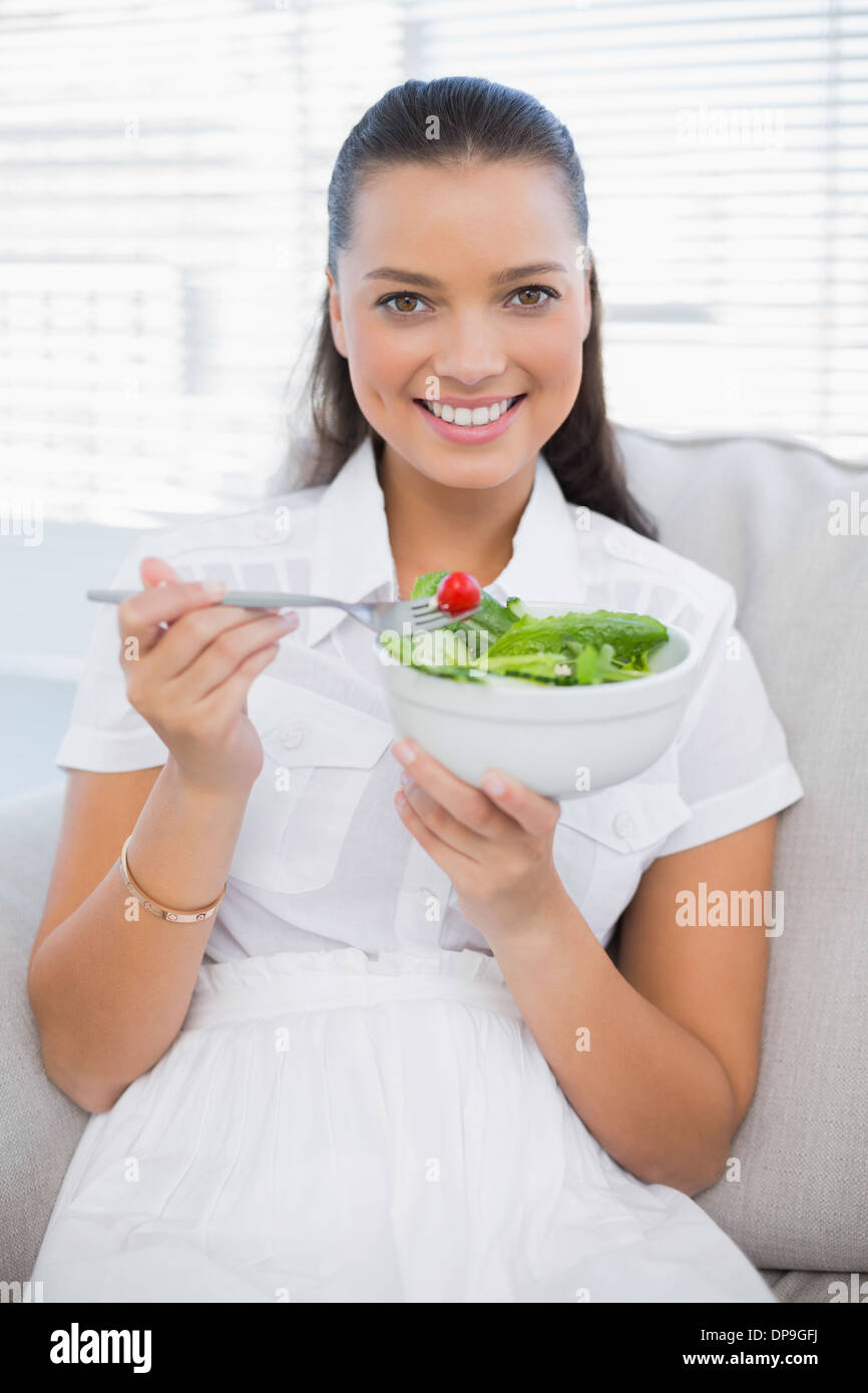 Smiling pretty woman eating healthy salad sitting on sofa Stock Photo ...