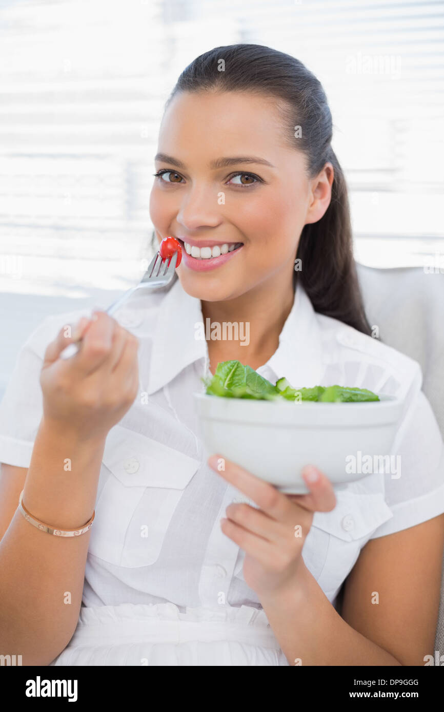 Cheerful pretty woman eating healthy salad sitting on sofa Stock Photo ...
