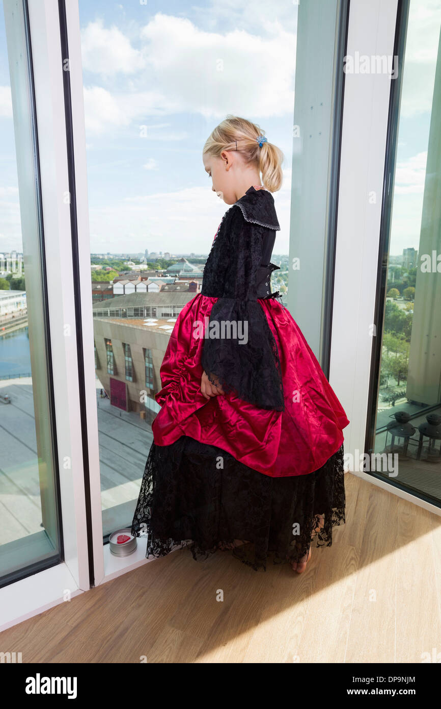 Full length of girl in vampire costume looking out through window at ...