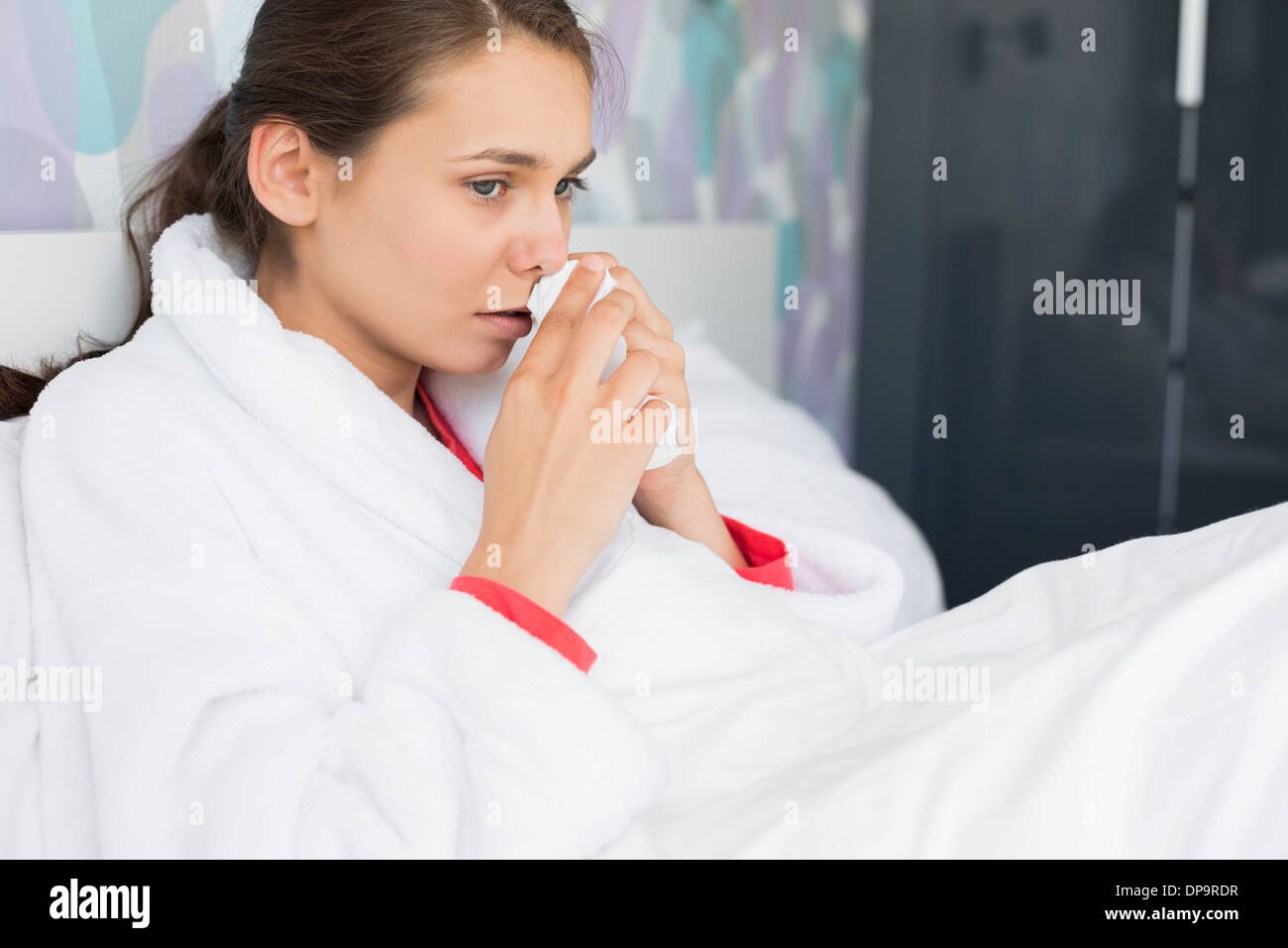 Young woman suffering from cold using tissue paper in bedroom Stock ...