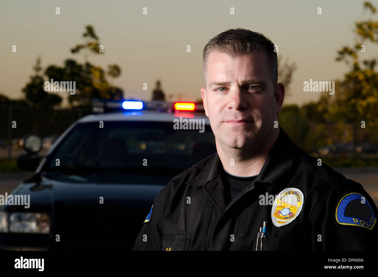 A serious looking police officer standing in his front of his patrol ...