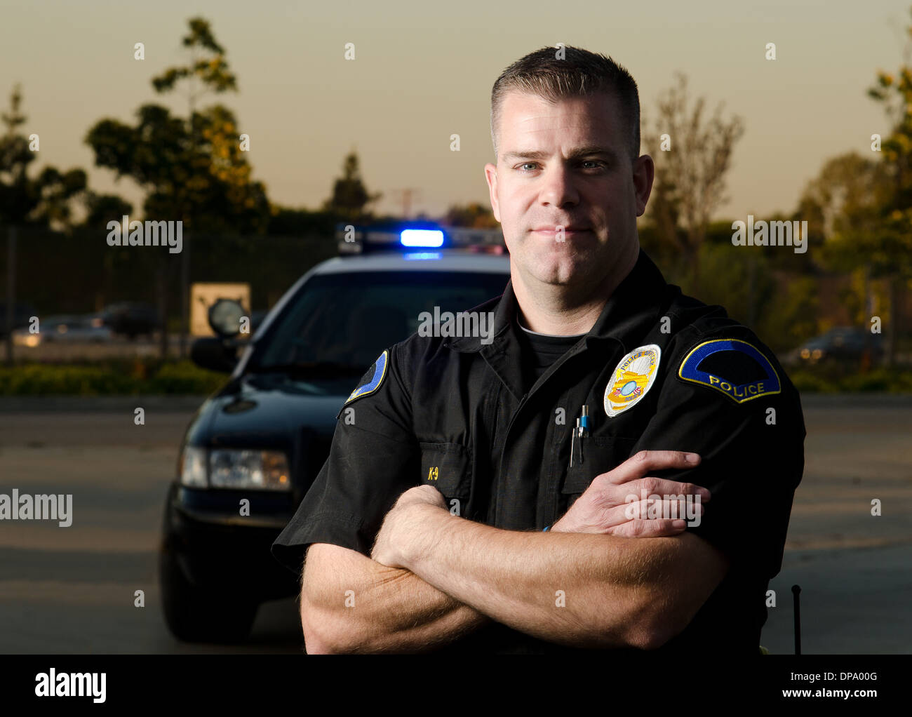 A strong looking police officer with his arms folded and his patrol car ...