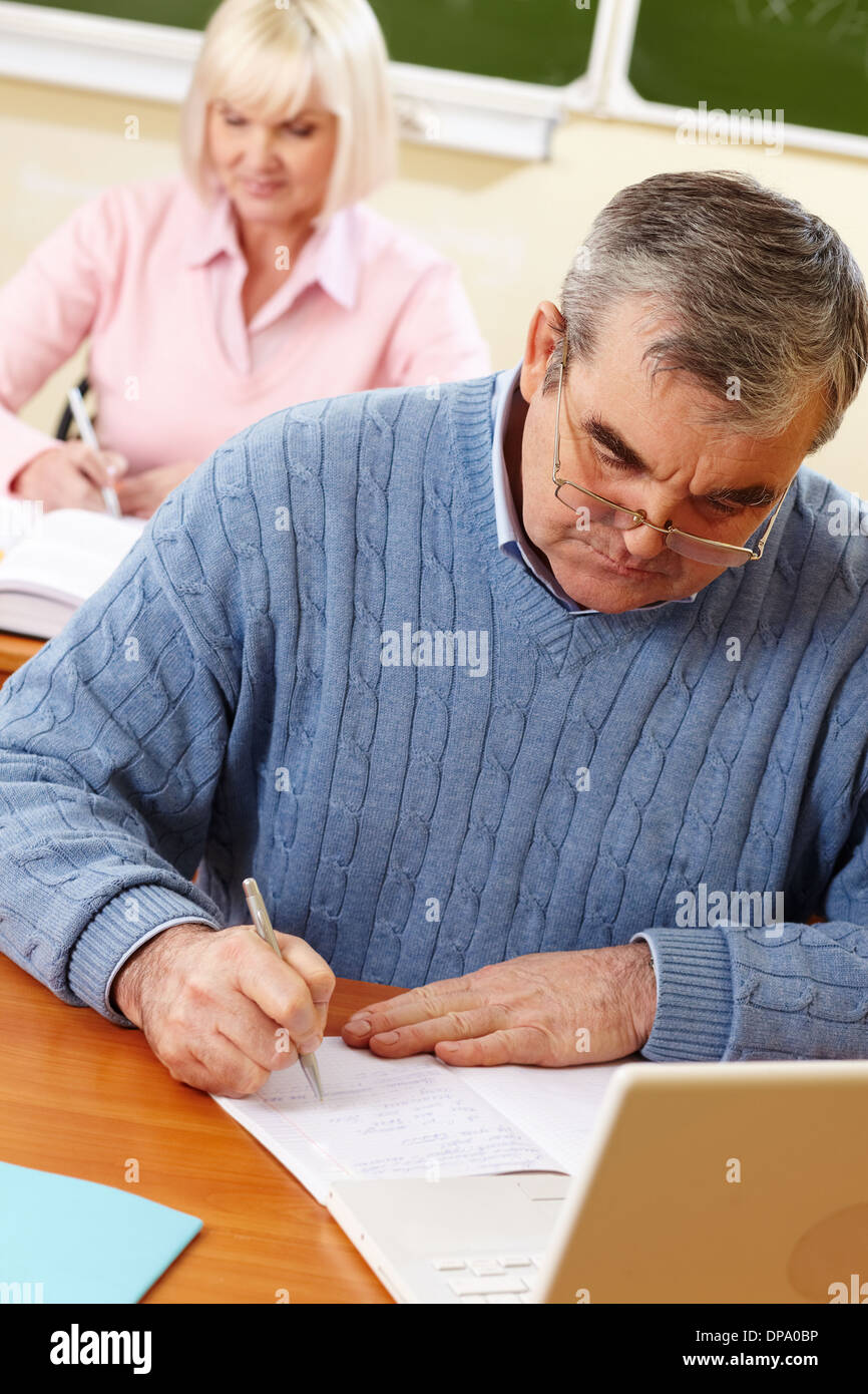 Senior man doing the task in classroom with his classmate on background ...