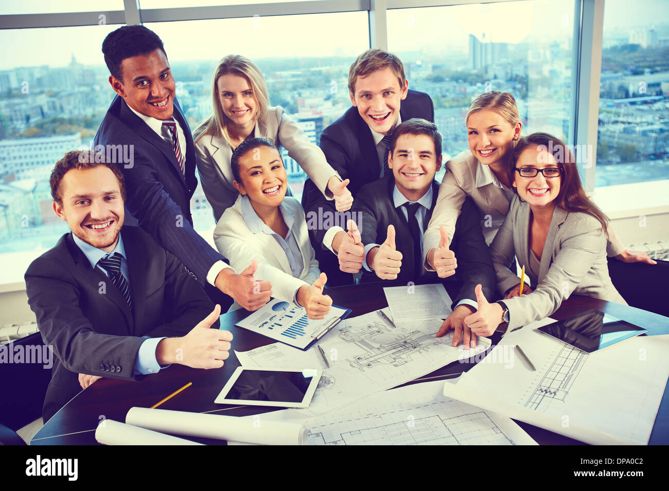 Group of business partners showing thumbs up while sitting at workplace ...