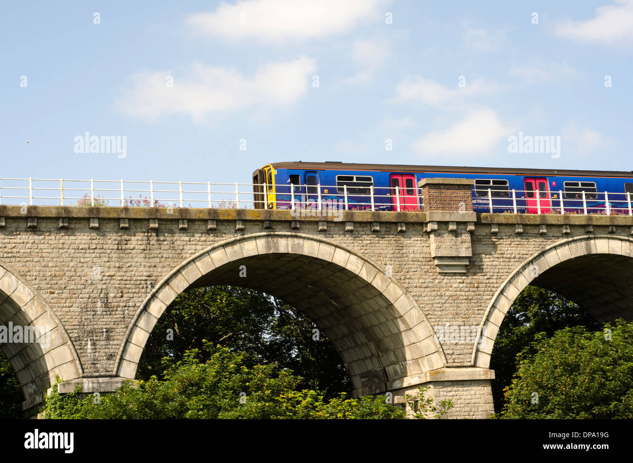 A brightly coloured train going over old stone bridge above tree tops ...