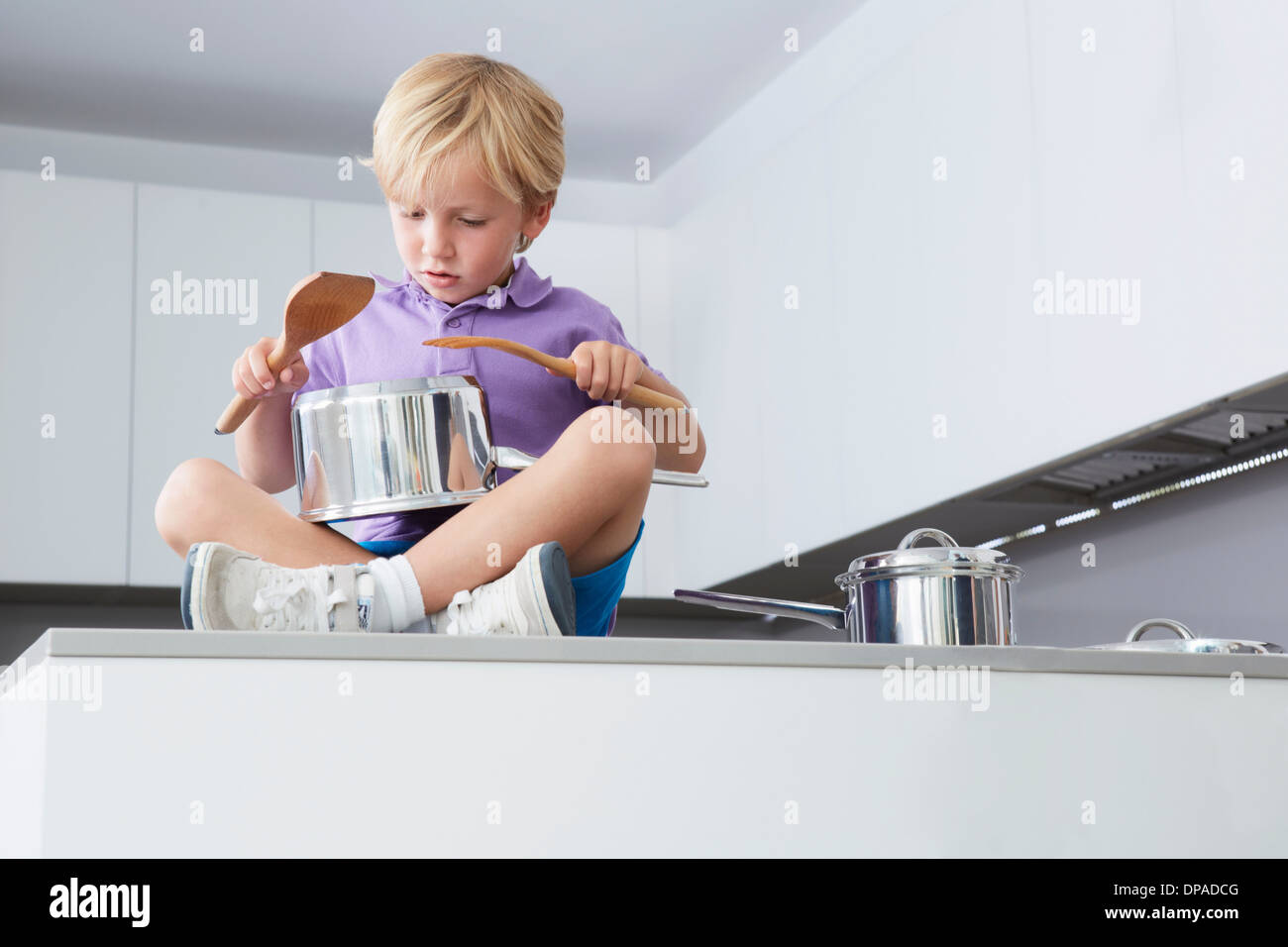 Boy sitting on kitchen counter playing drums with pans and wooden ...