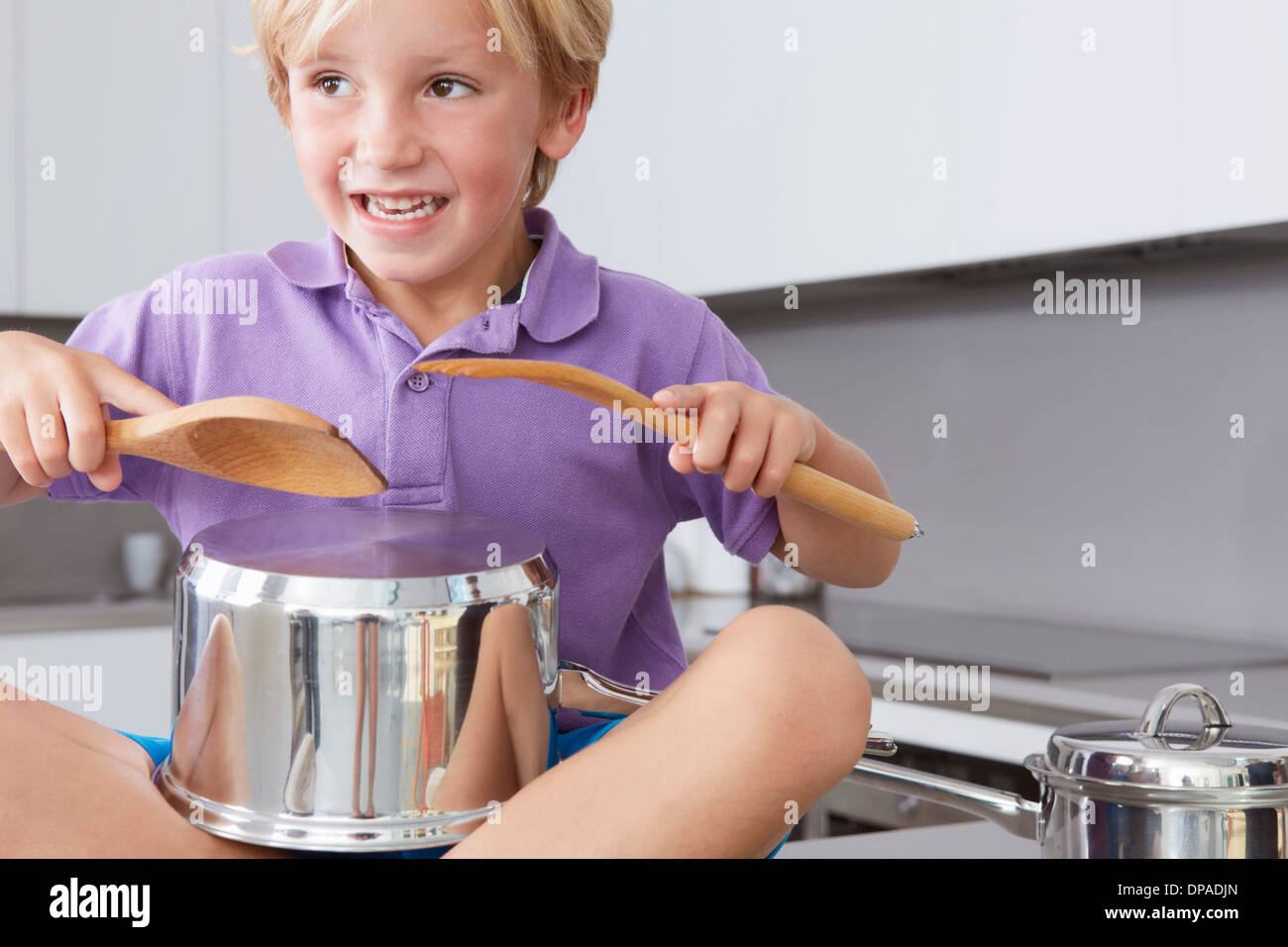 Boy sitting on kitchen counter playing drums with pans and wooden ...