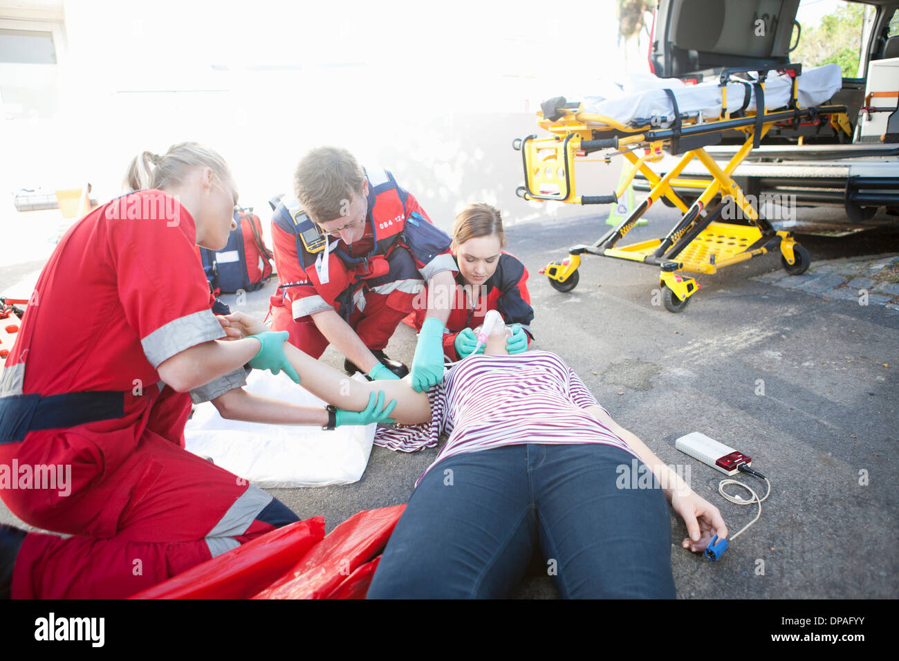 Three paramedics tending patient on road Stock Photo - Alamy