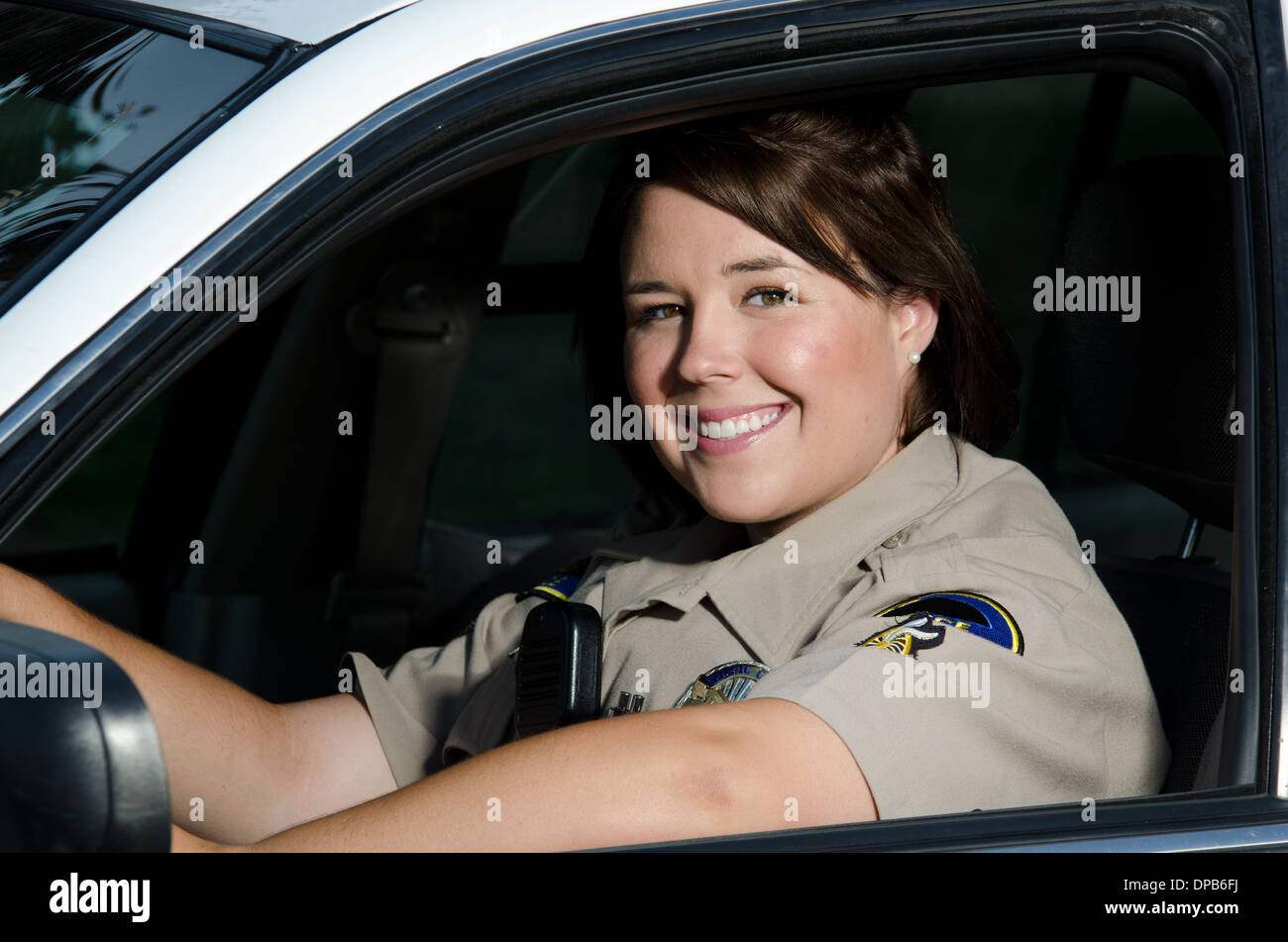 a friendly looking female police officer sits and smiles in her patrol ...