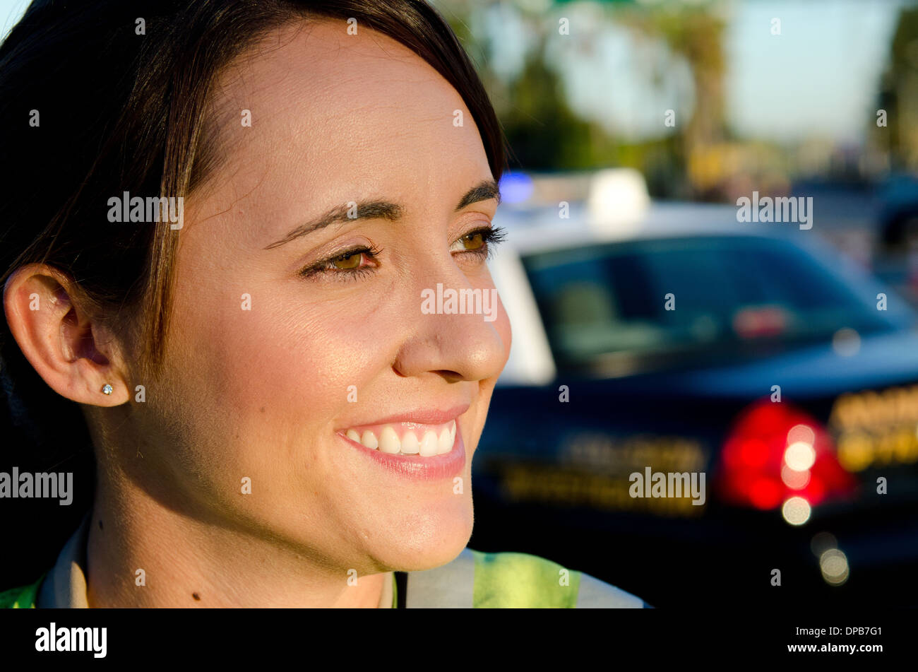 a close up of a smiling female police officer with her patrol car in ...