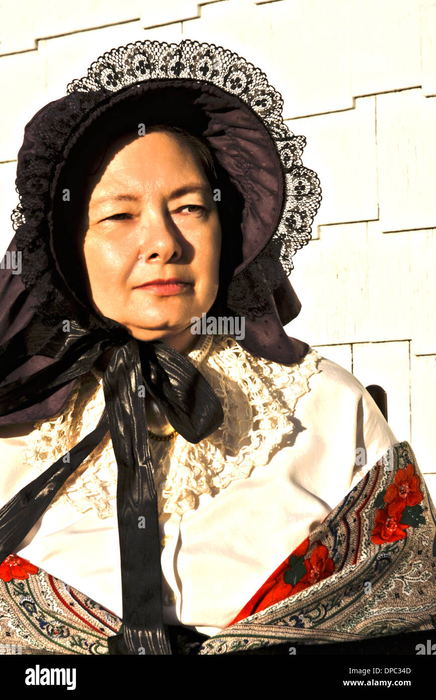 A lady wearing a bonnet dressed in 1800s time period on a house porch ...