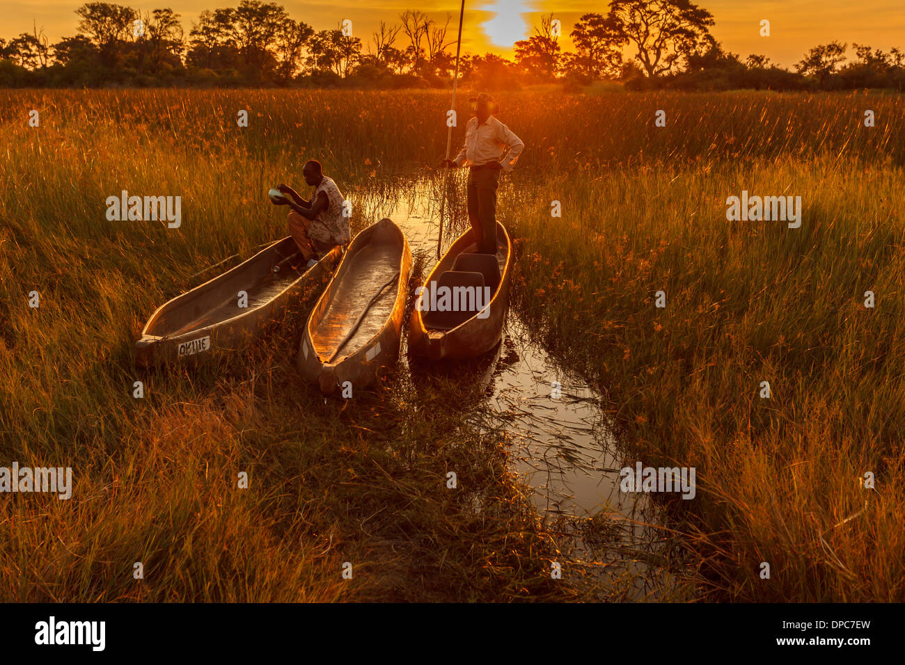 Two native men with makoro dugout canoes highlighted by orange glow of ...