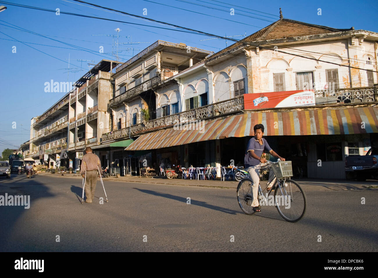 A man riding a bicycle passes a man walking with crutches on a city ...