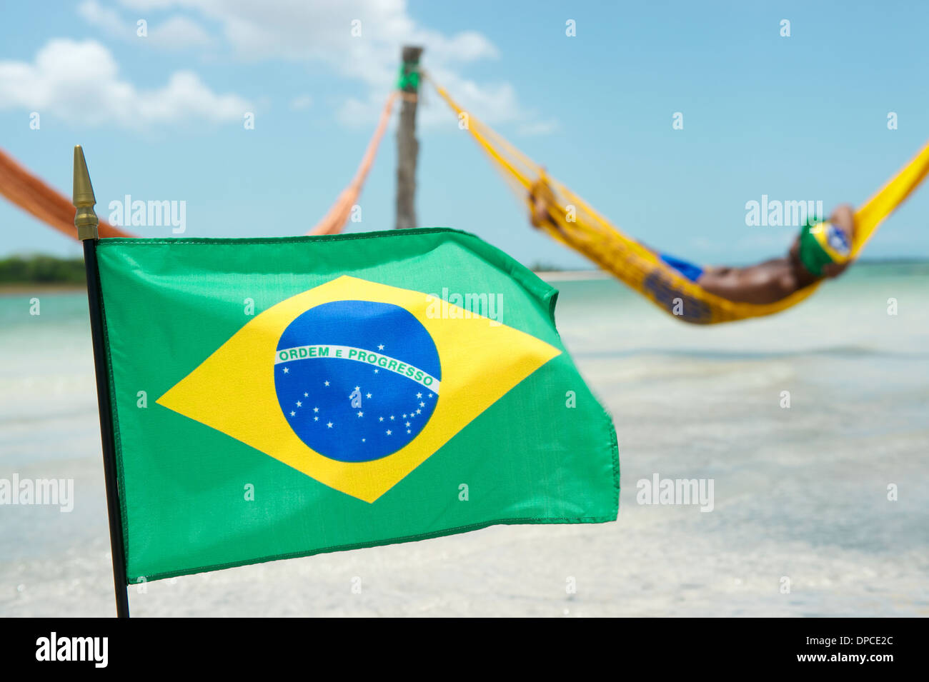 Brazilian flag waving in front of man relaxing in beach hammock strung ...
