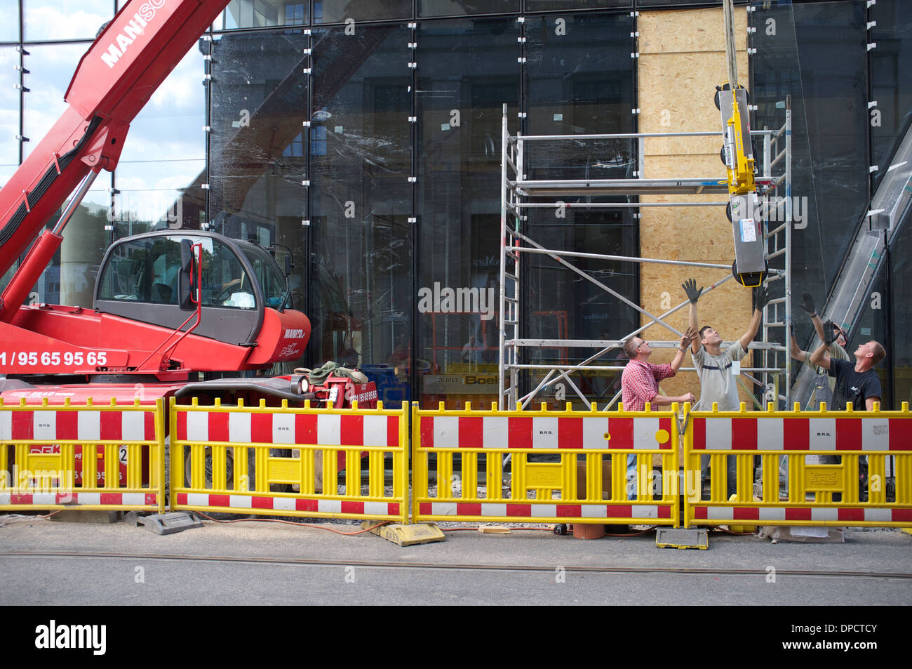 Construction workers fitting large glass panels to a shopping centre ...