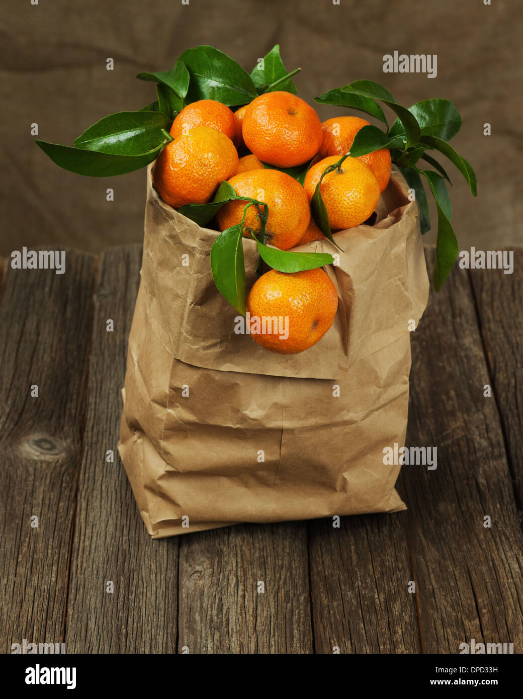 Fresh tangerines with leaves in recycle paper bag on wooden table ...