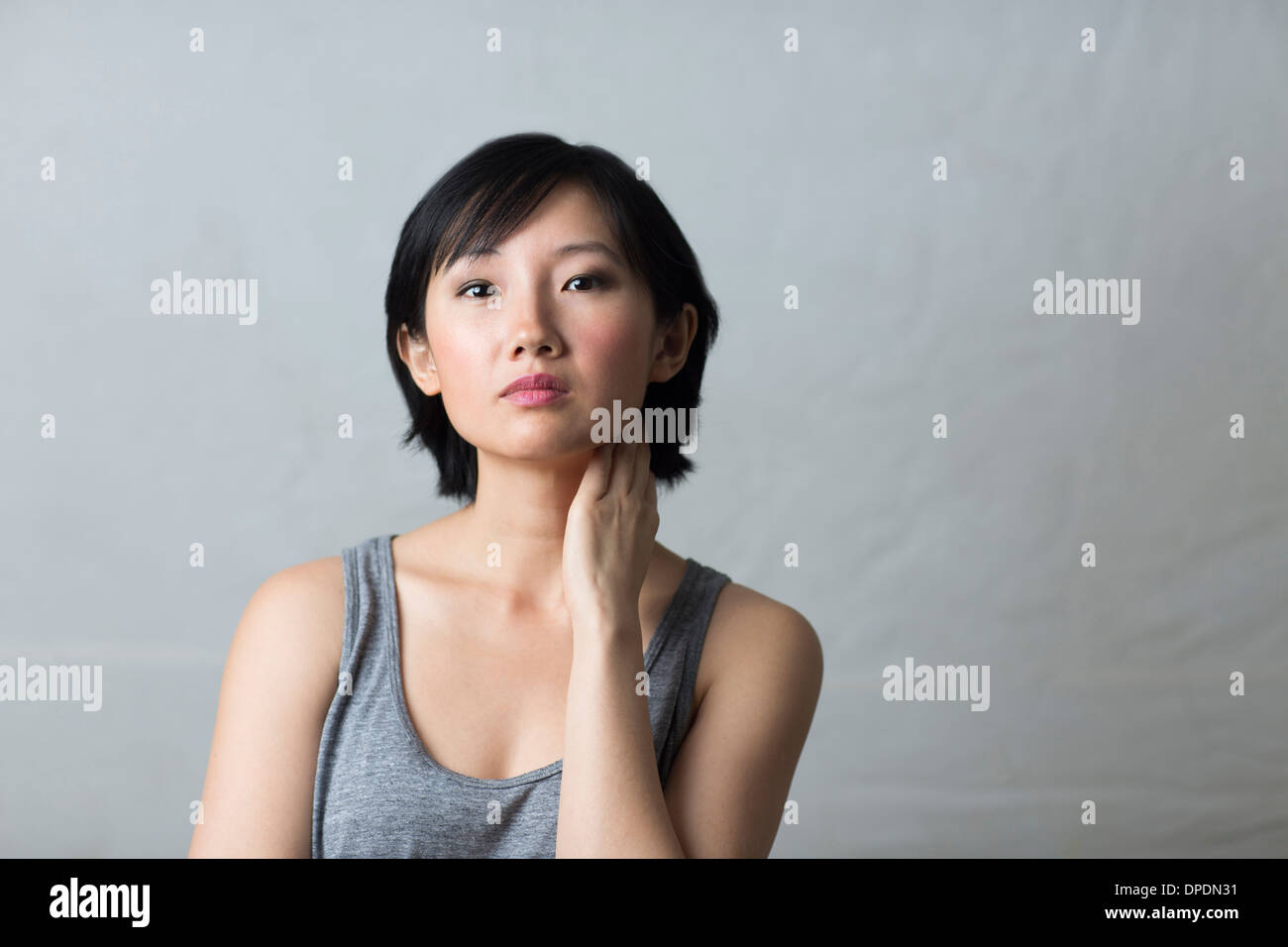 Studio portrait of young woman with hand on neck Stock Photo - Alamy