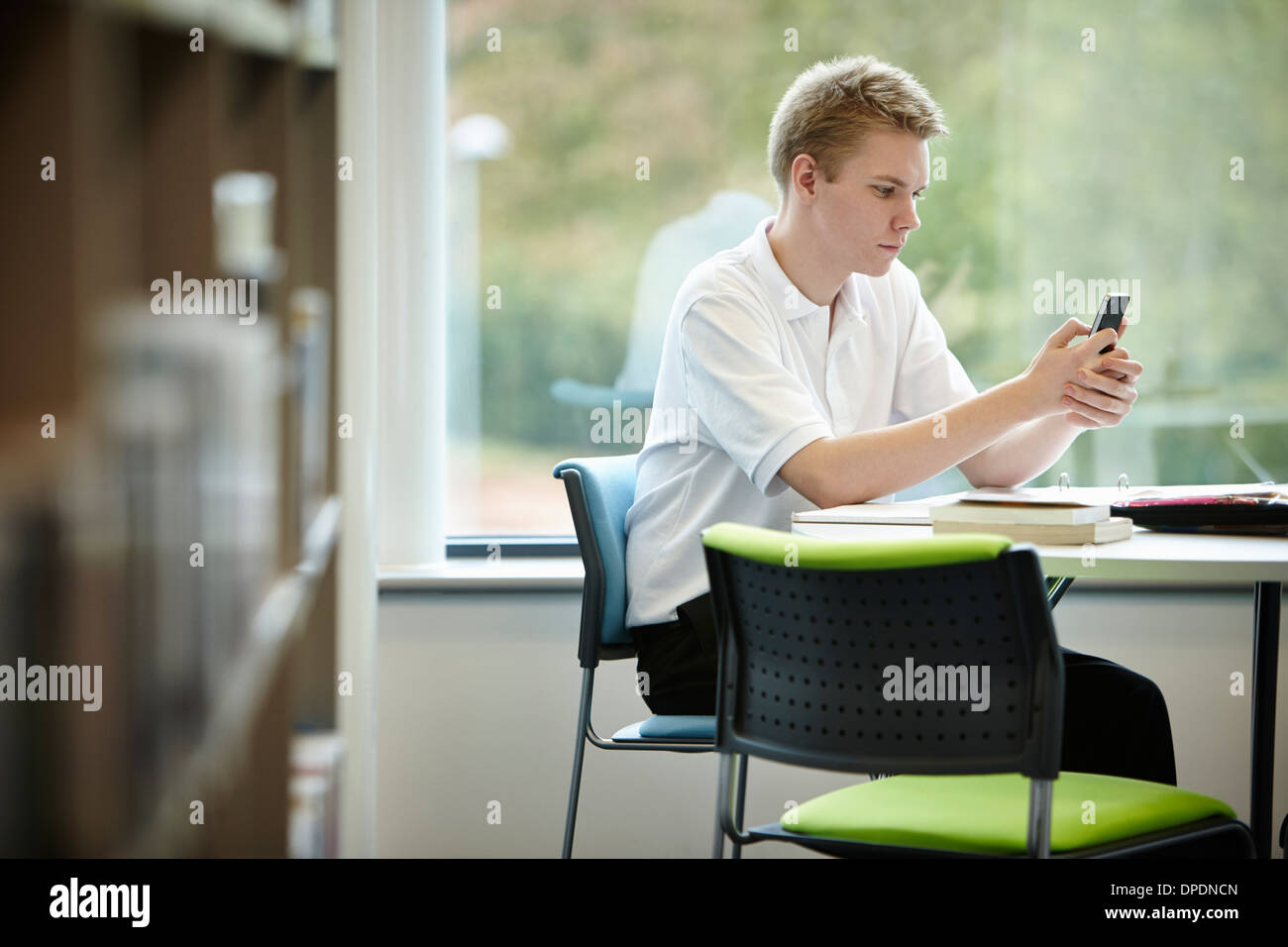 Teenage boy using cell phone in library Stock Photo - Alamy