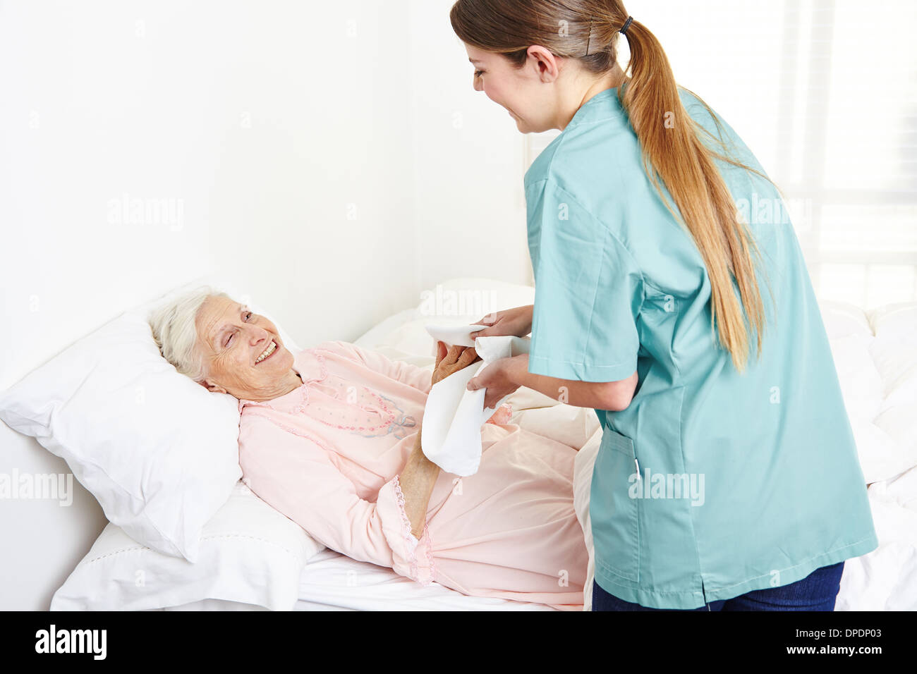 Geriatric nurse washing bedridden senior woman and drying her hands in ...