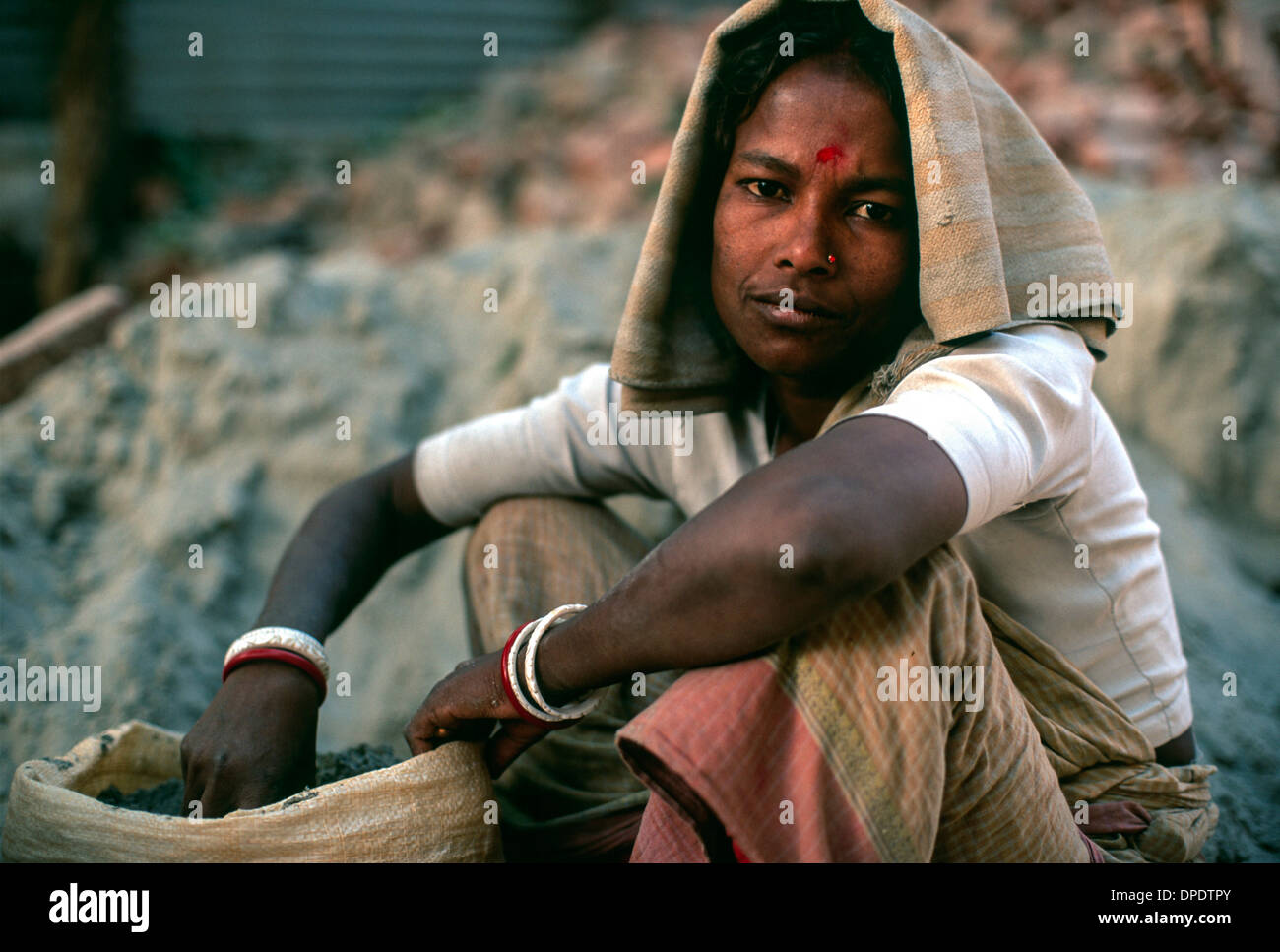 Young woman of low caste sits taking a moments rest in the heat of her ...