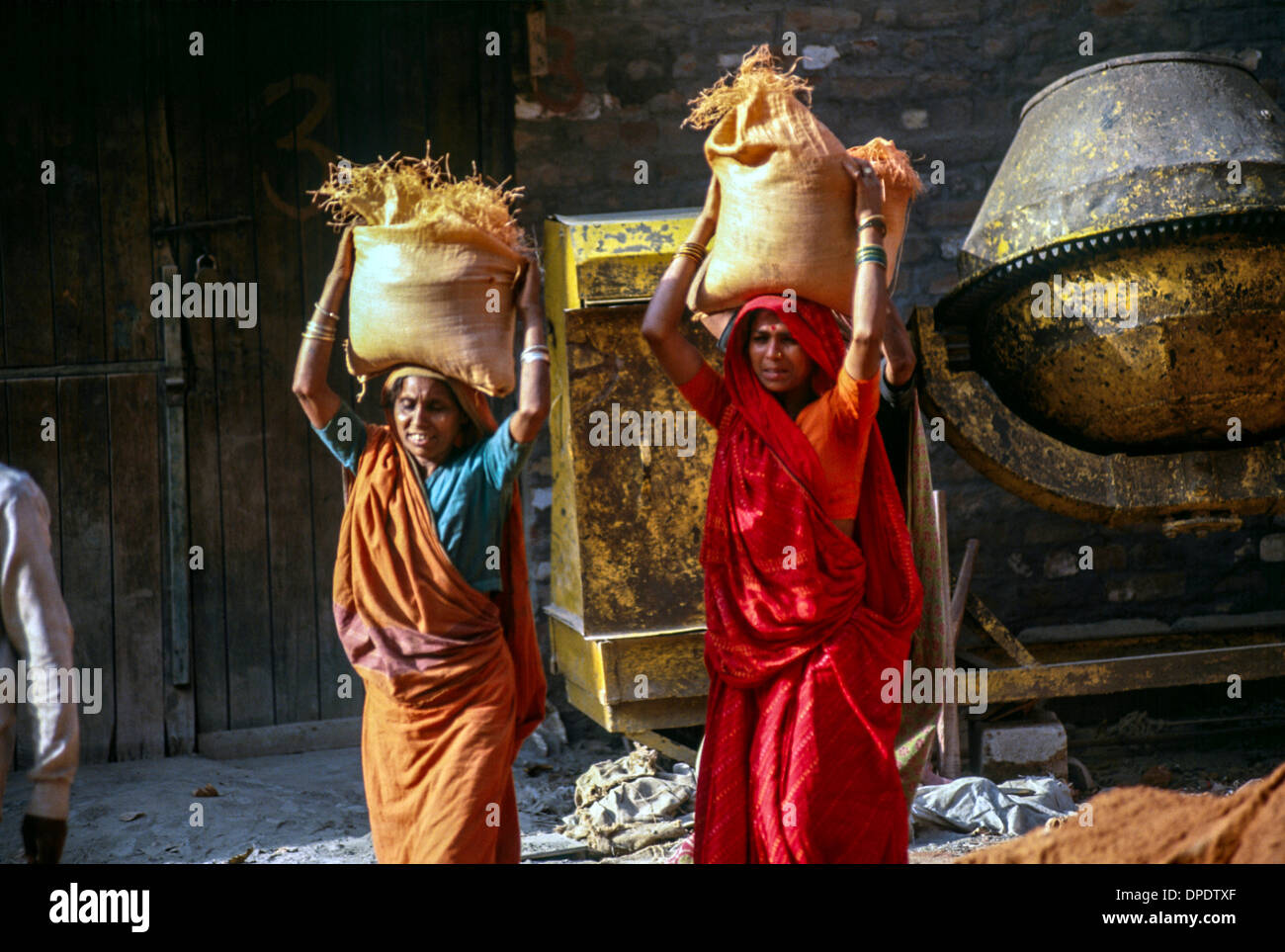 Two young women workers carry sacks of building material on their heads ...