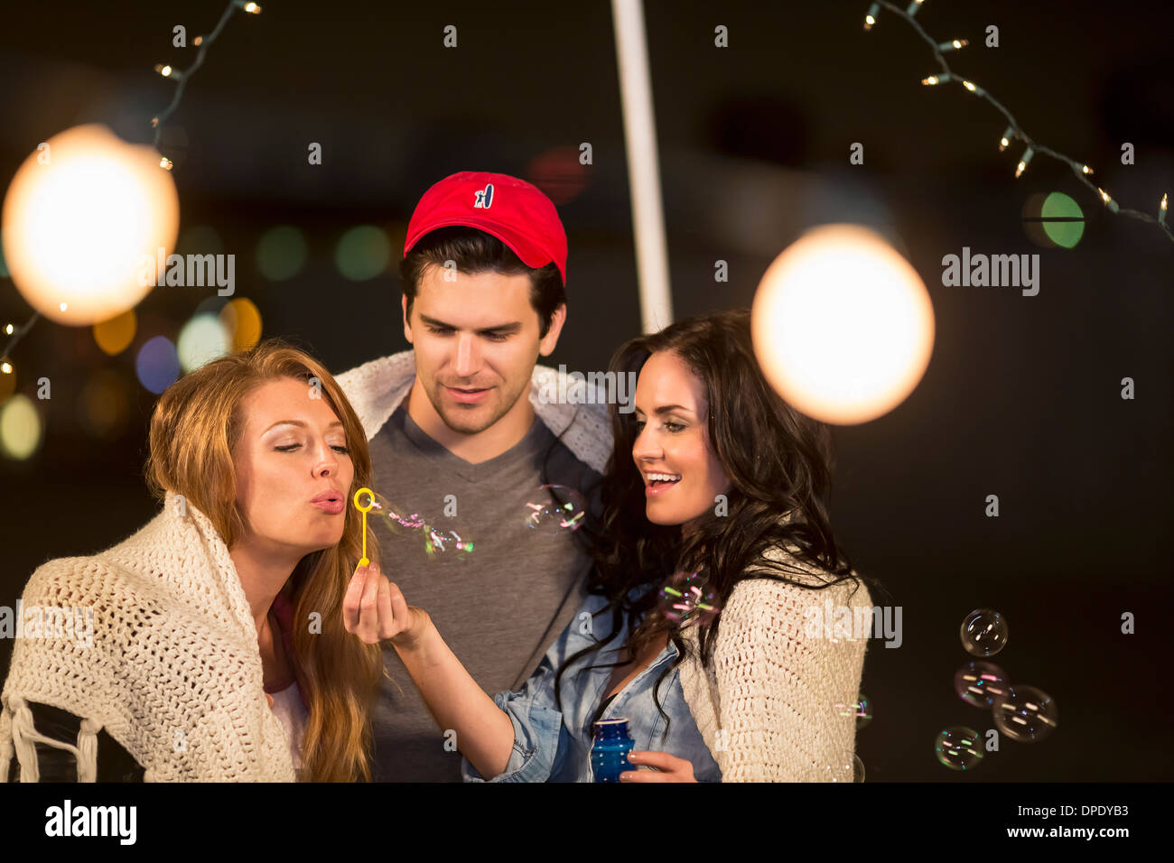 Young adult friends fooling around blowing bubbles at rooftop party ...