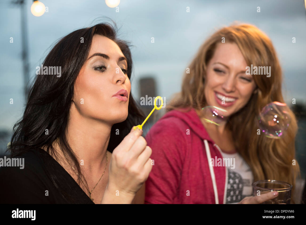 Two female friends blowing bubbles at rooftop party Stock Photo - Alamy