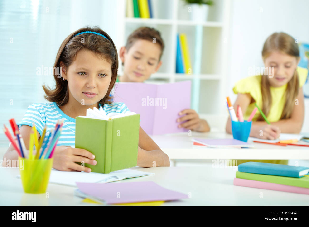 Portrait of lovely girl looking in notepad with her two schoolmates on ...
