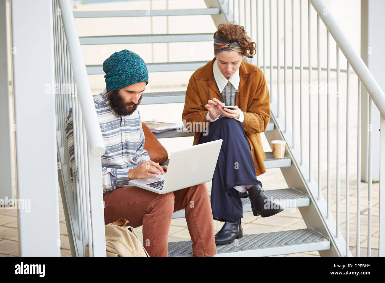 Hipster couple using computer and smartphone at university campus Stock ...