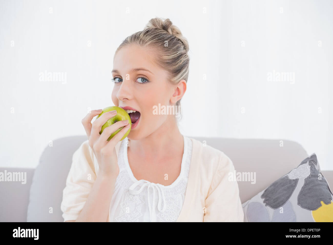 Gorgeous model eating green apple sitting on sofa Stock Photo - Alamy