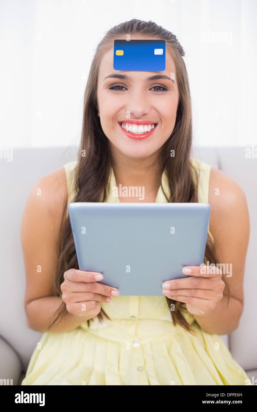 Happy brunette with credit card on forehead holding tablet Stock Photo ...