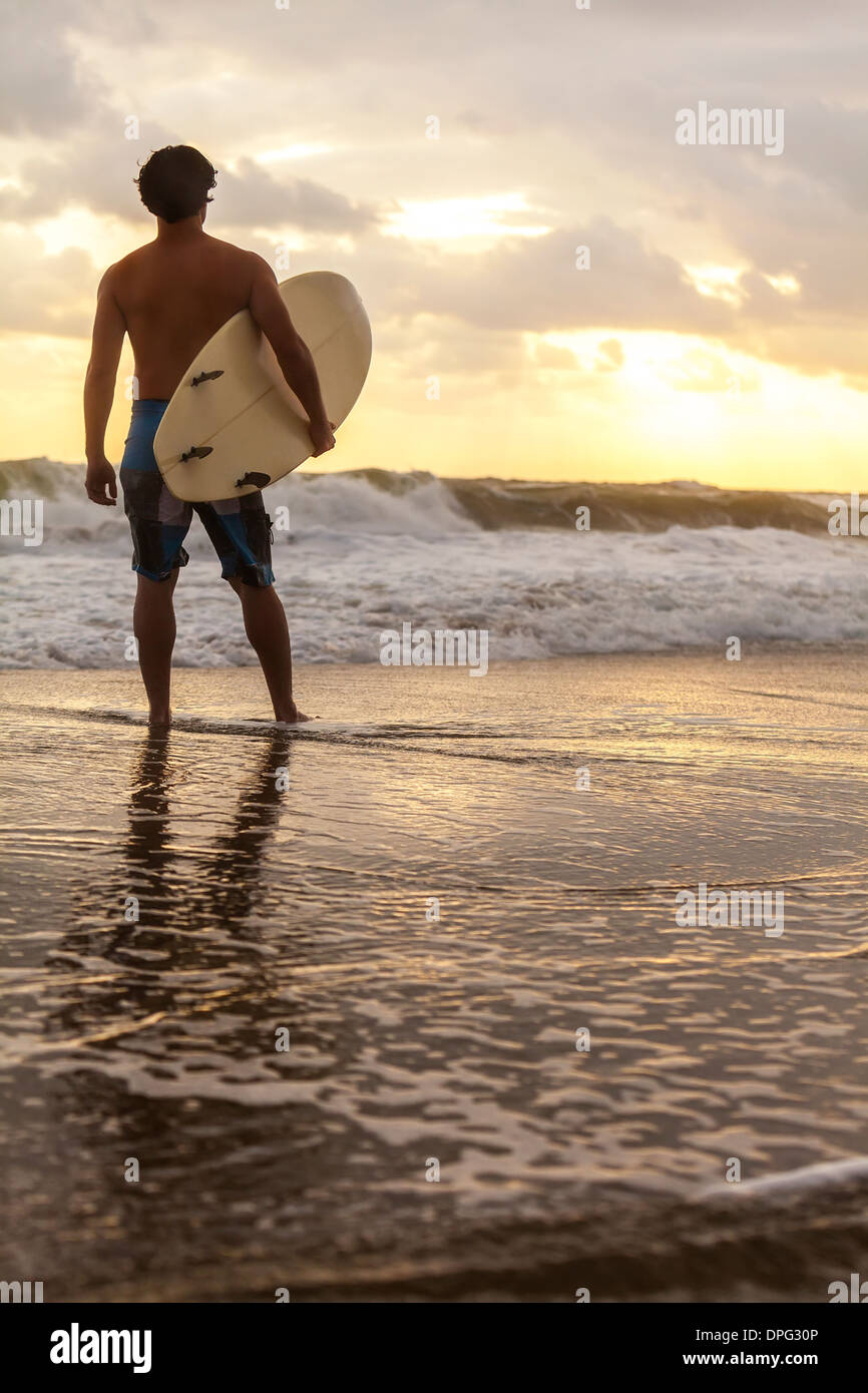 Rear view of male surfer with white surfboard standing on a beach at ...