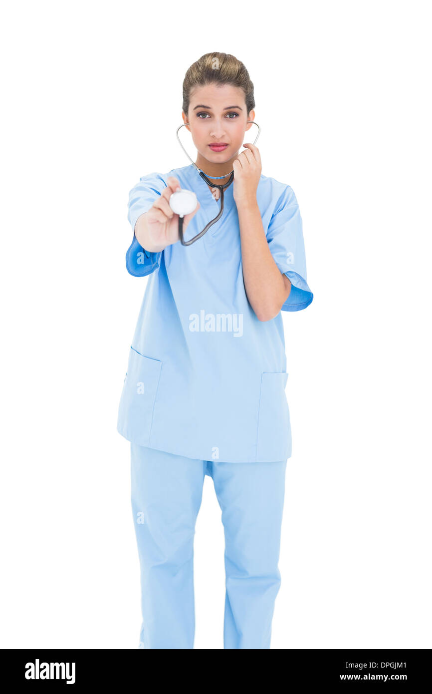 Stern brown haired nurse in blue scrubs using a stethoscope Stock Photo ...