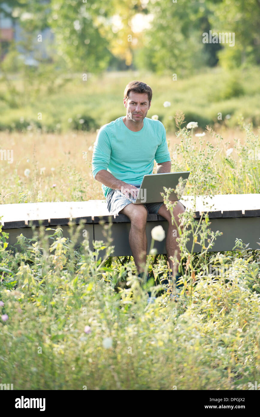 Man using laptop computer while sitting out in countryside Stock Photo ...