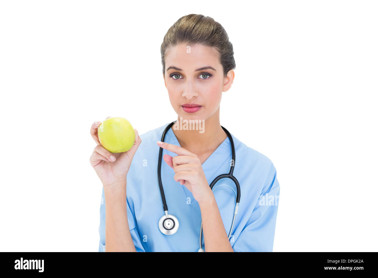Stern brown haired nurse in blue scrubs pointing an apple with her ...