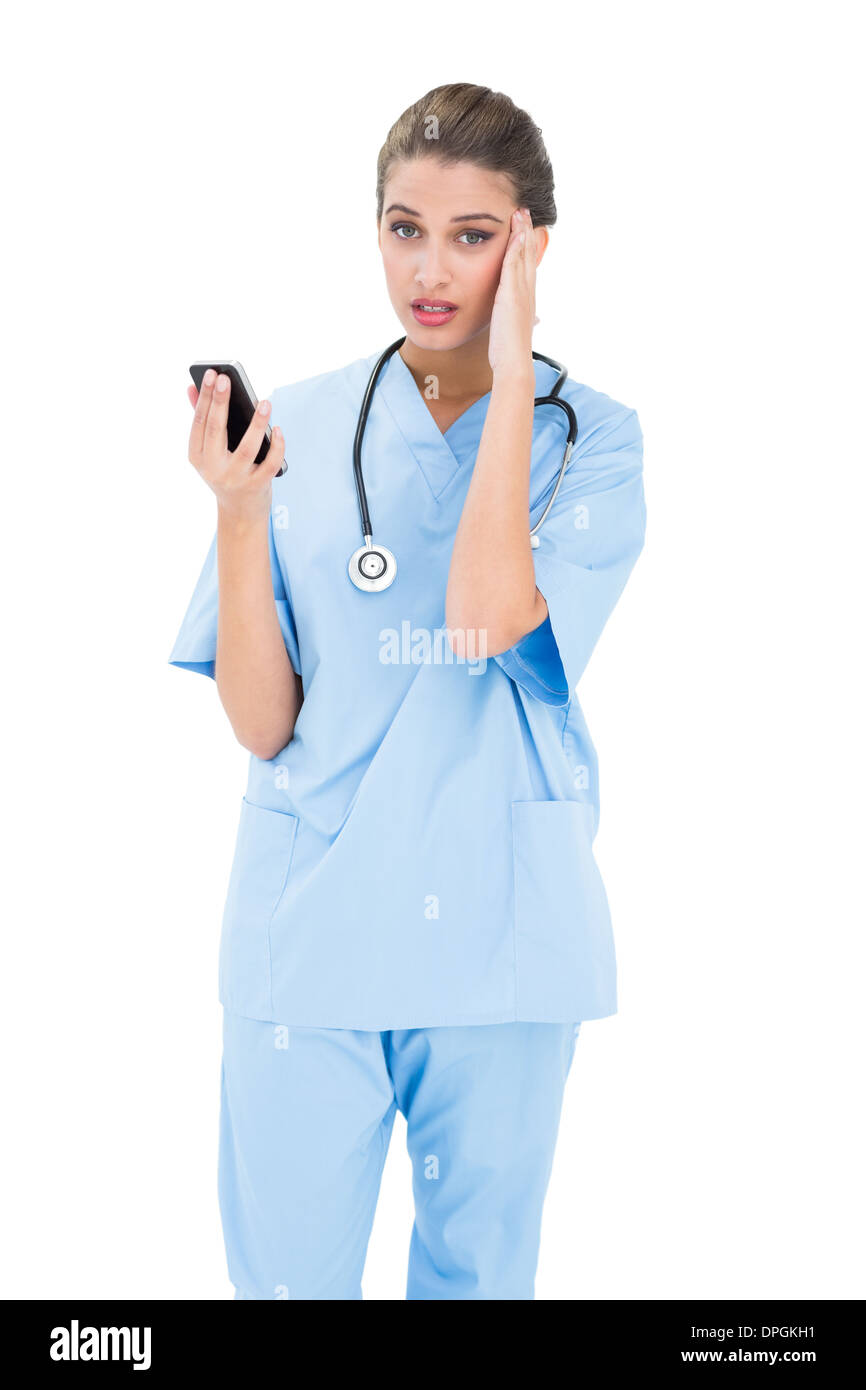 Confused brown haired nurse in blue scrubs using a mobile phone Stock ...