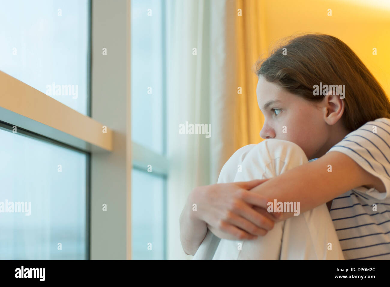 Preteen girl hugging knees, looking out window Stock Photo - Alamy