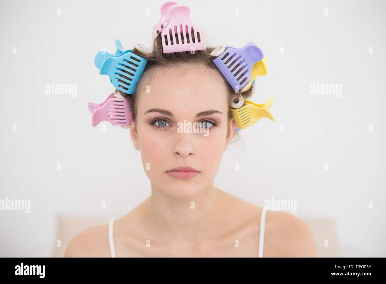 Stern natural brown haired woman in hair curlers looking at camera ...